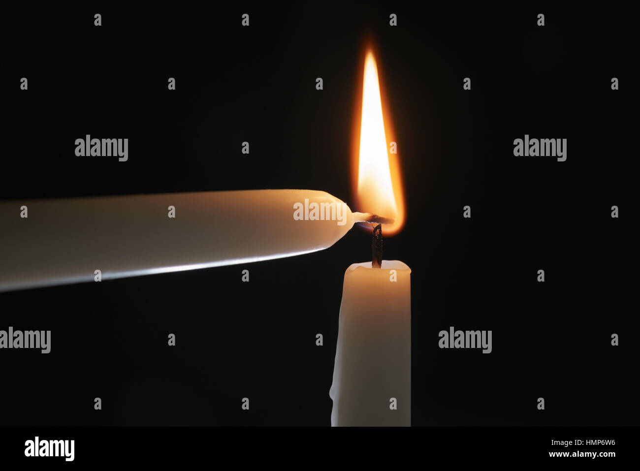 ighting tall candle with another candle in the dark Stock Photo - Alamy