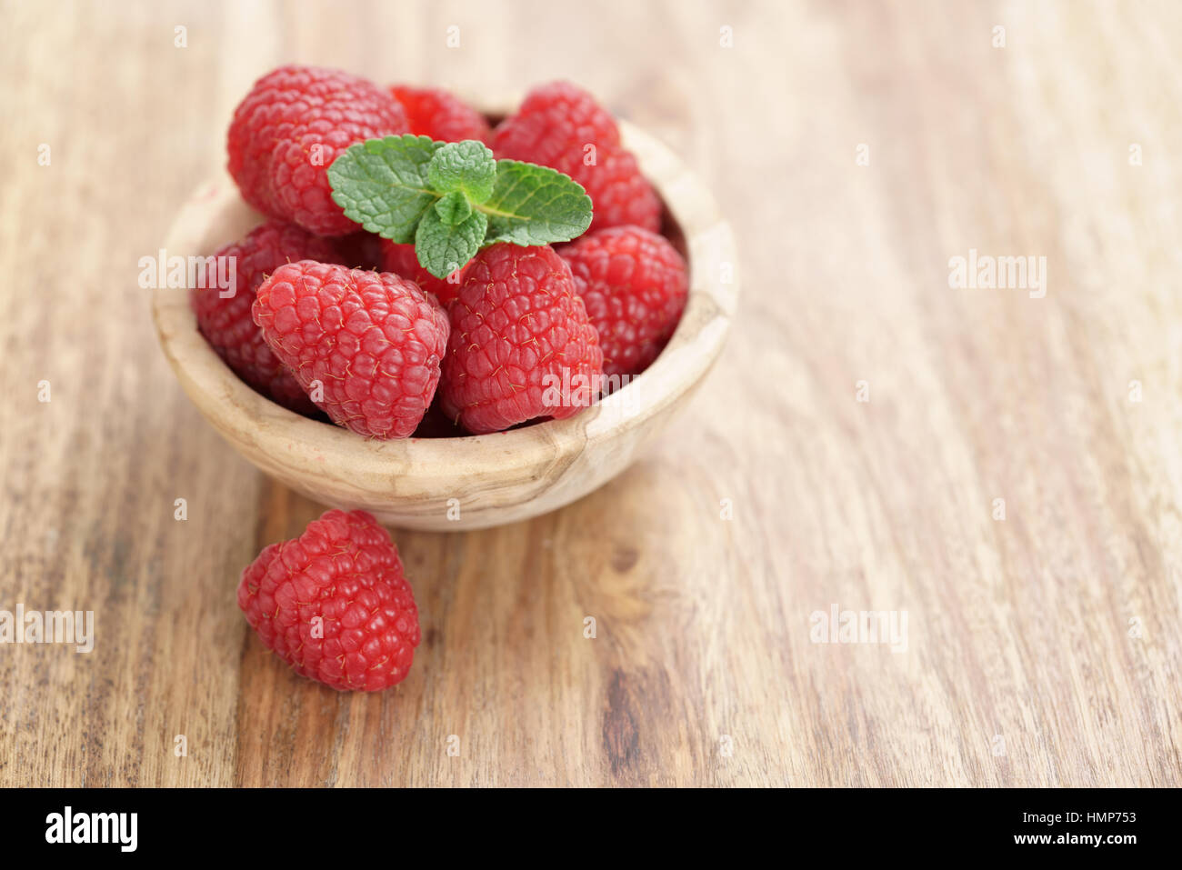 wood bowl full of ripe raspberries with mint leaves on old wooden table ...