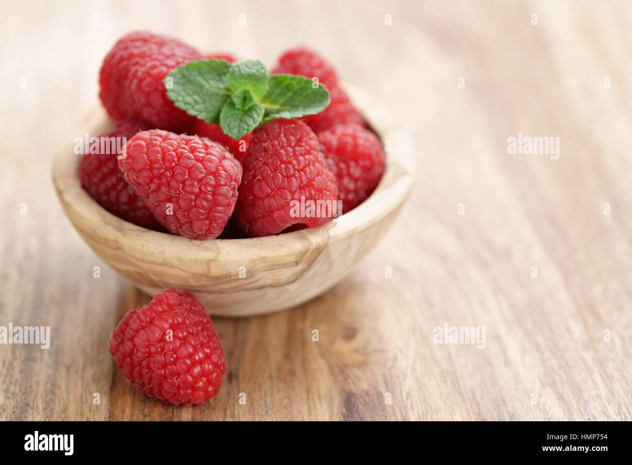wood bowl full of ripe raspberries with mint leaves on old wooden table ...