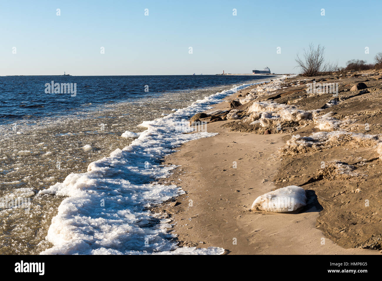 frozen beach near shipyard and sea port with rays of sun and ...