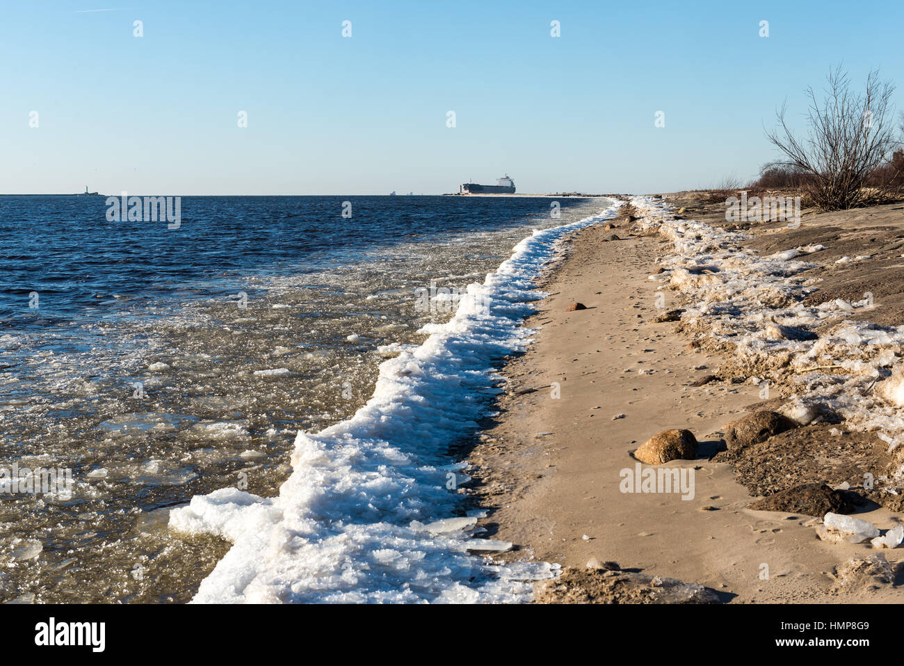 frozen beach near shipyard and sea port with rays of sun and ...
