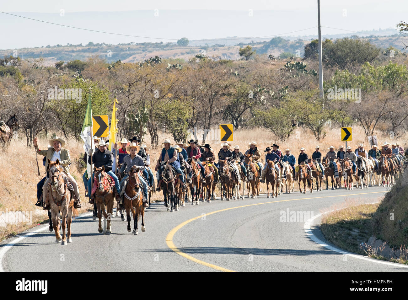 Mexican cowboys ride along a stretch of highway though the high desert ...