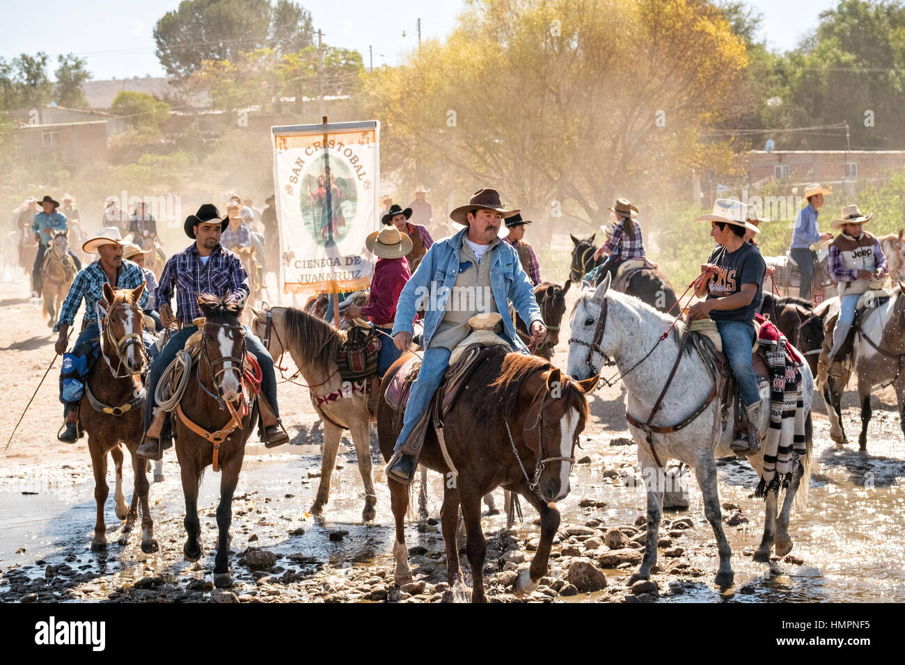 Mexican cowboys ride across a stream to water their horses on their way ...