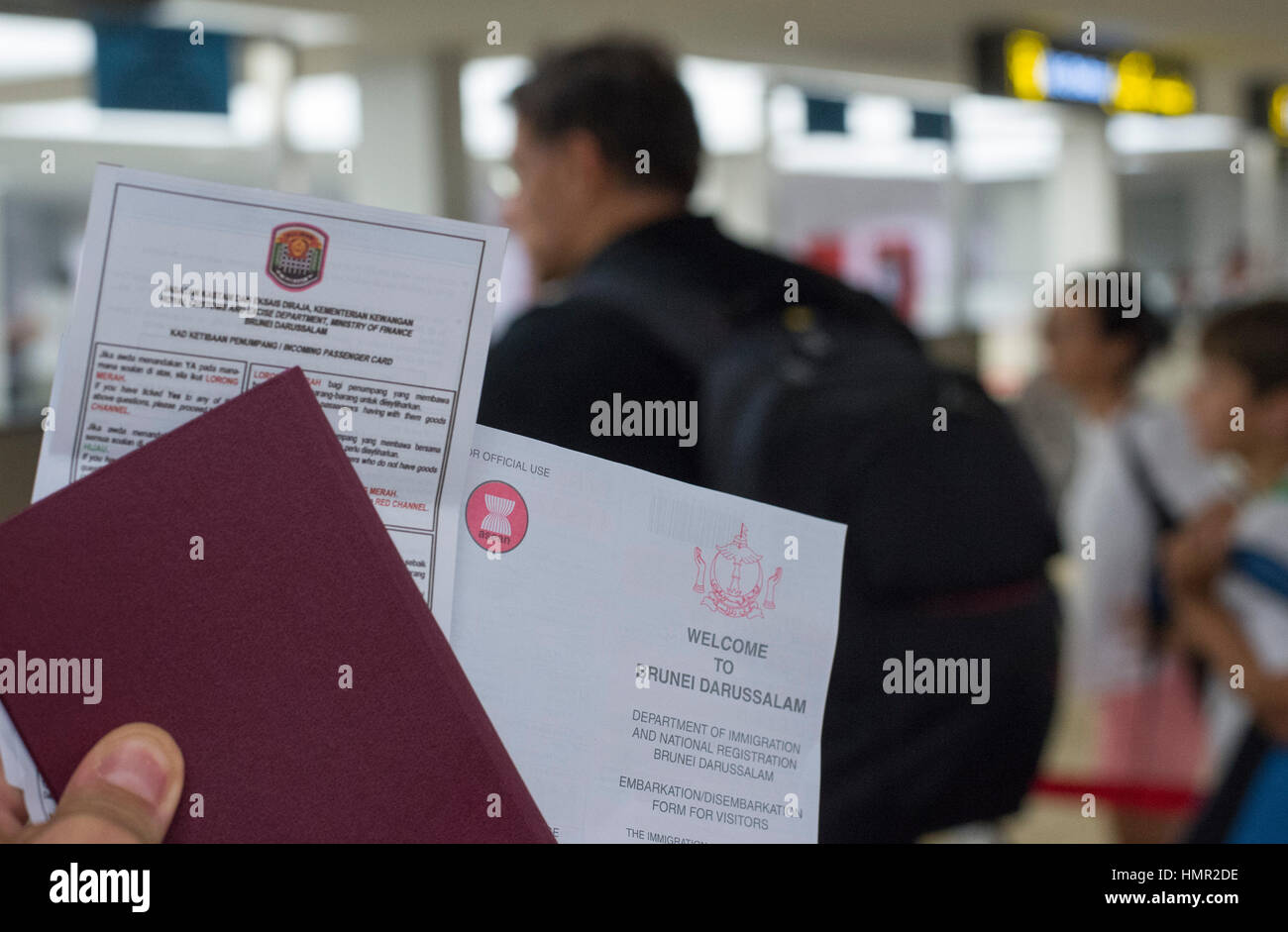 A red passport is held with the Arrival Card of Brunei immigration ...
