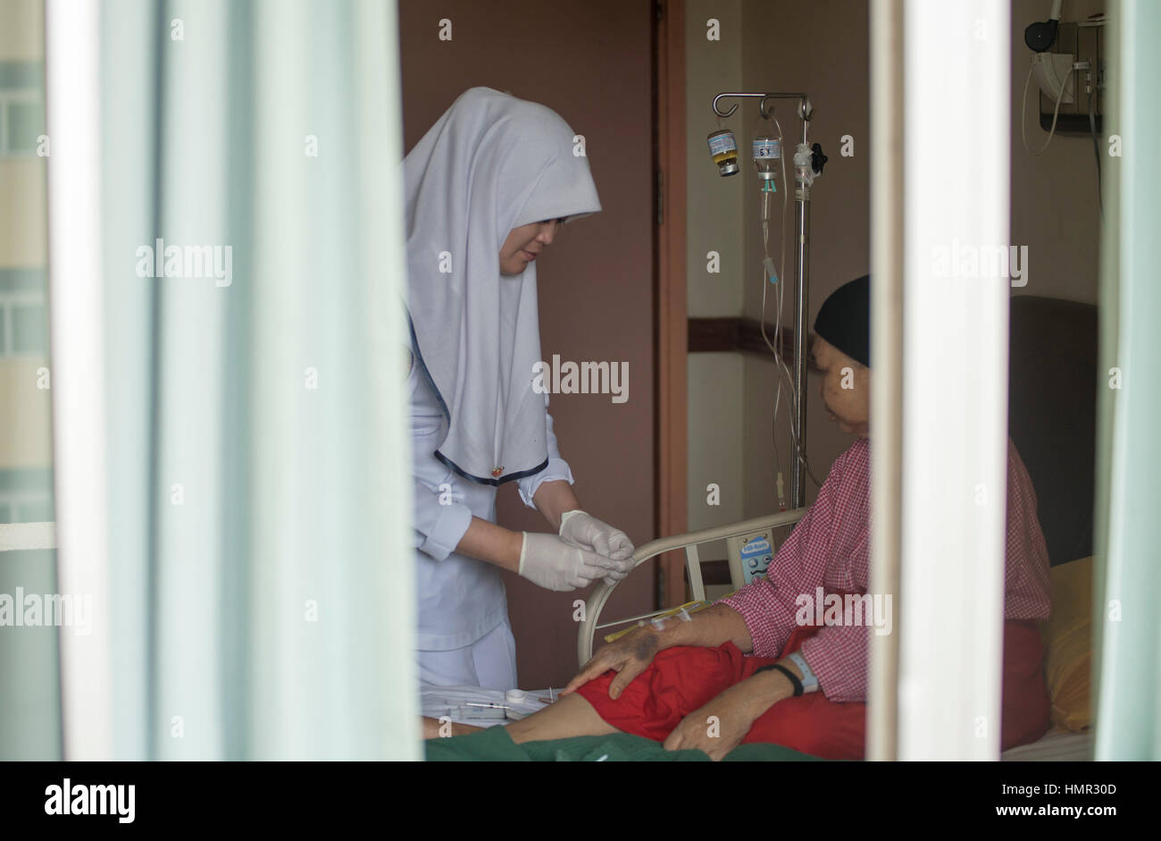 A nurse wearing a headscarf or hijab is administering a drip to an ...