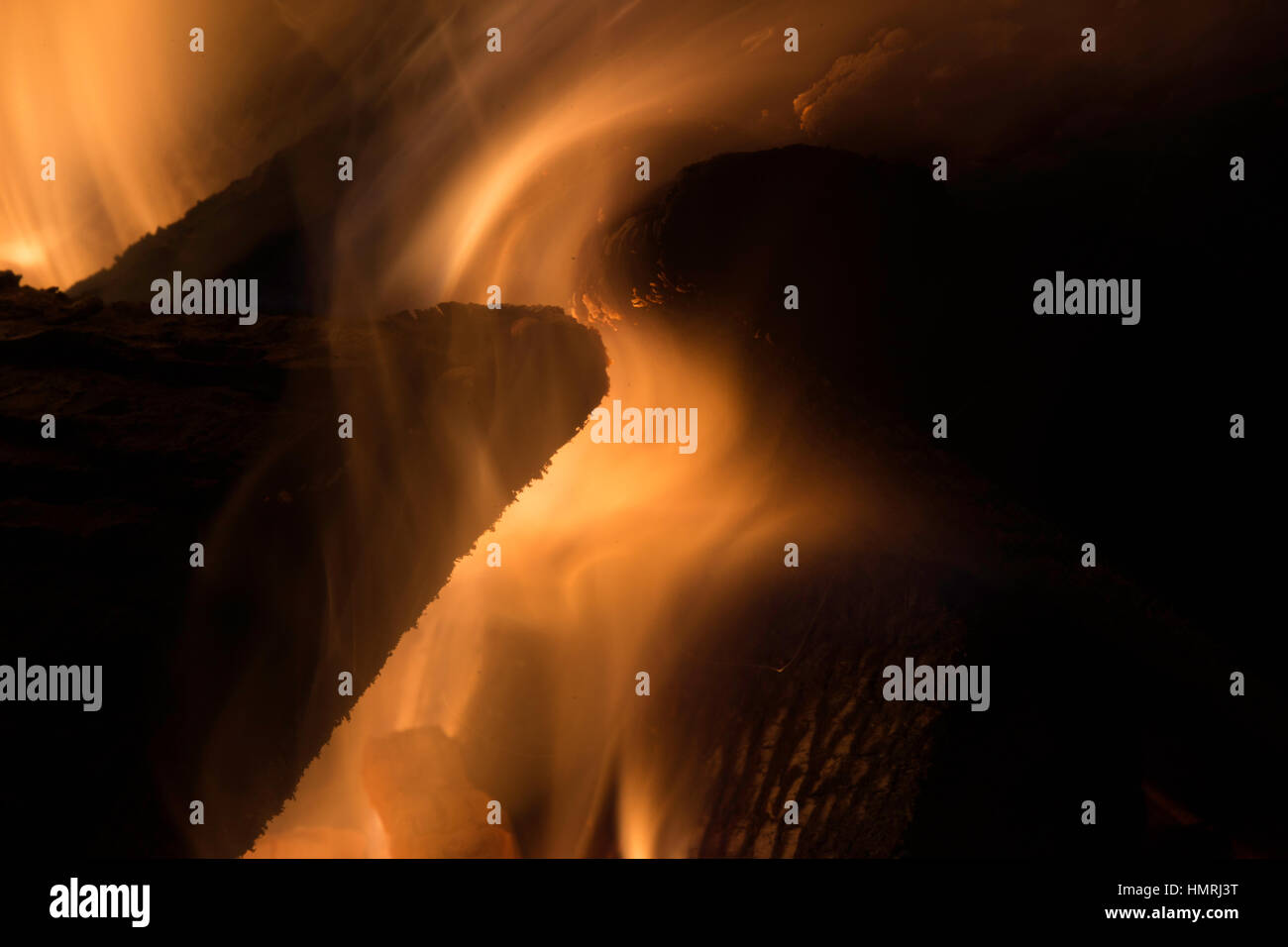 Flames curling, rising and glowing around wood logs, smoky closeup ...