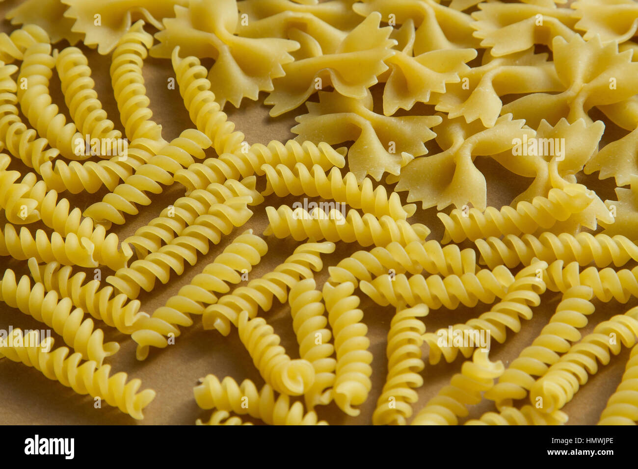 Bow and spiral shape pasta on brown background close view Stock Photo ...