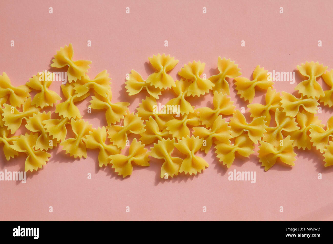 Maсaroni or pasta bow shape in row on pink background Stock Photo - Alamy