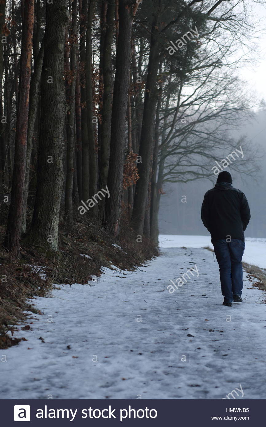 A man dressed in winter clothes and cap goes walking on an icy path in ...