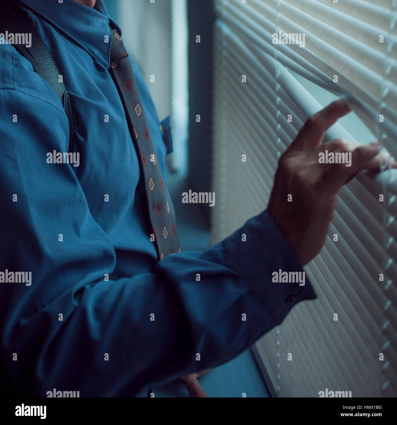 Pensive man thinking of something behind venetian blind, makes the gap ...