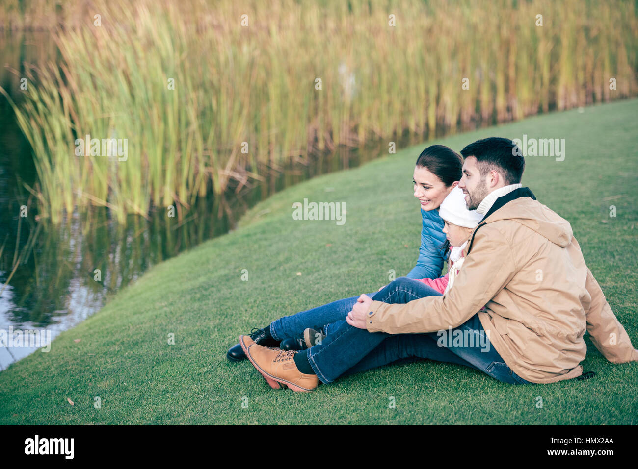 Smiling family sitting near lake Stock Photo - Alamy