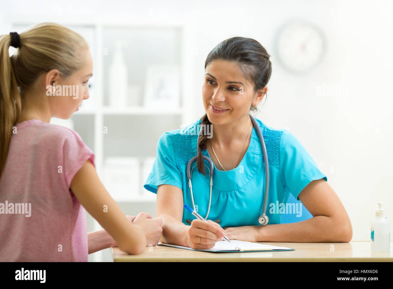 Young woman doctor talking to her teenager patient and writing down the ...
