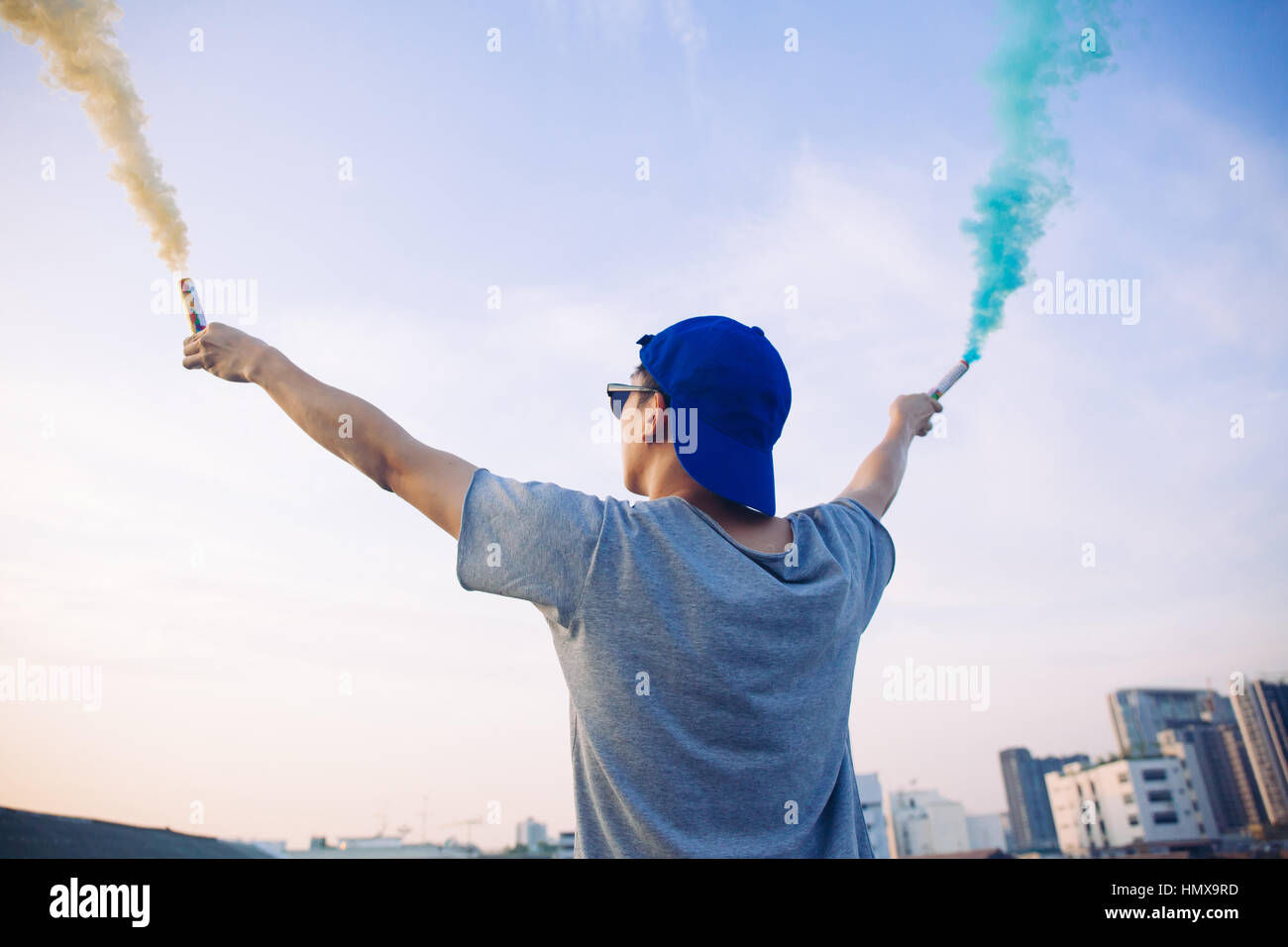 Male teenager holding colorful smoke sticks up in the air over urban ...