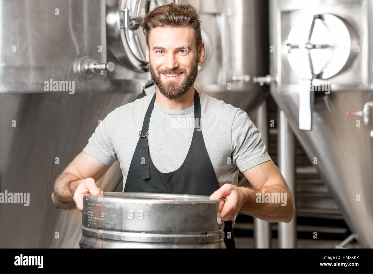 Worker carrying barrel with beer at the brewery with metal containers ...