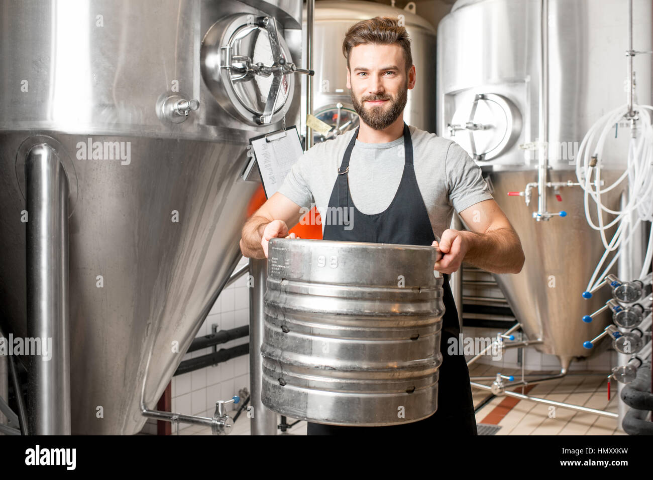 Worker carrying barrel with beer at the brewery with metal containers ...