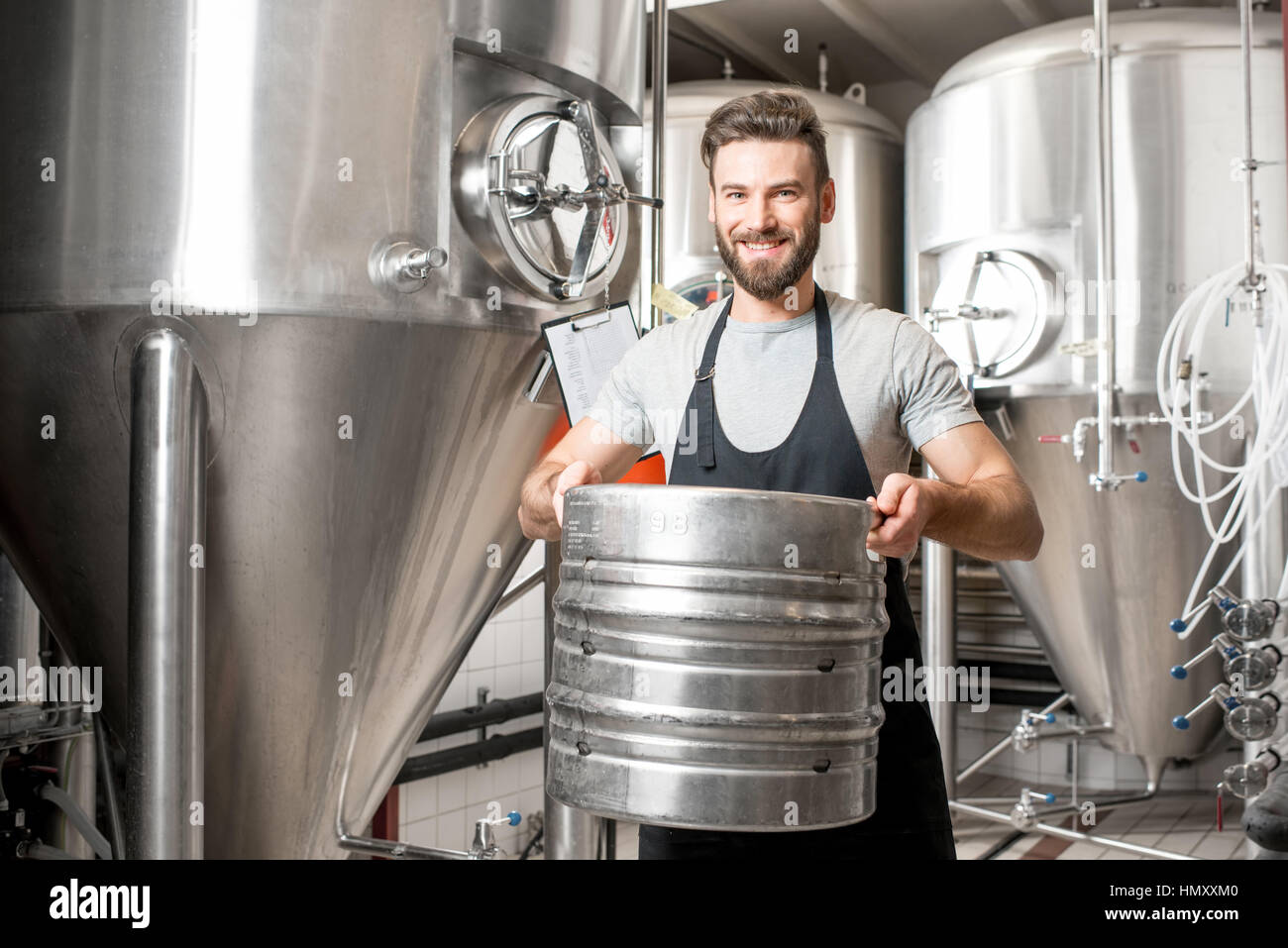 Worker carrying barrel with beer at the brewery with metal containers ...