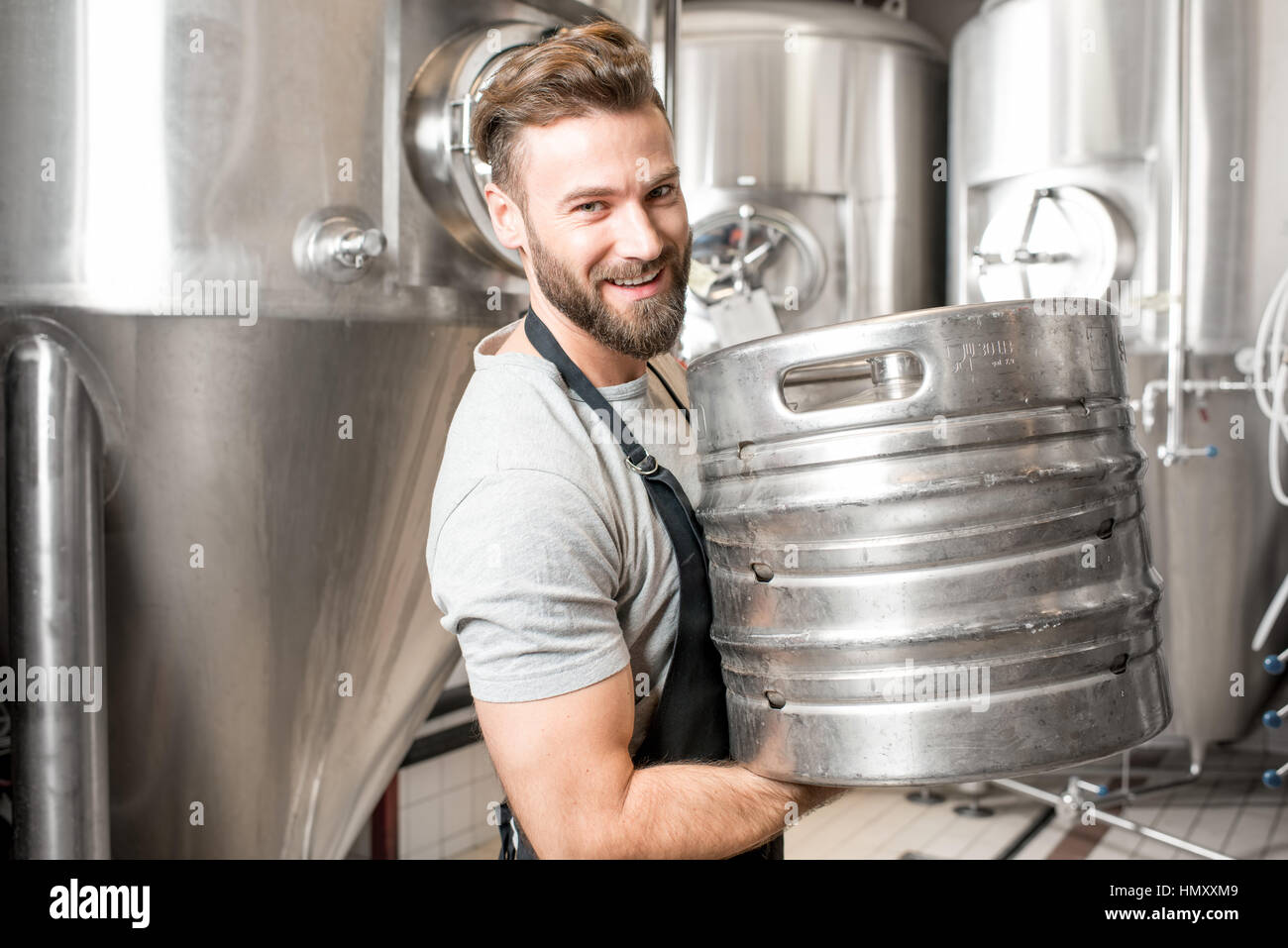 Worker carrying barrel with beer at the brewery with metal containers ...