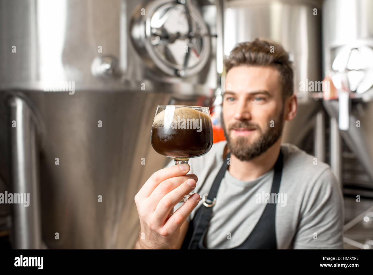 Handsome brewer in uniform checking quality of the beer sitting in the ...