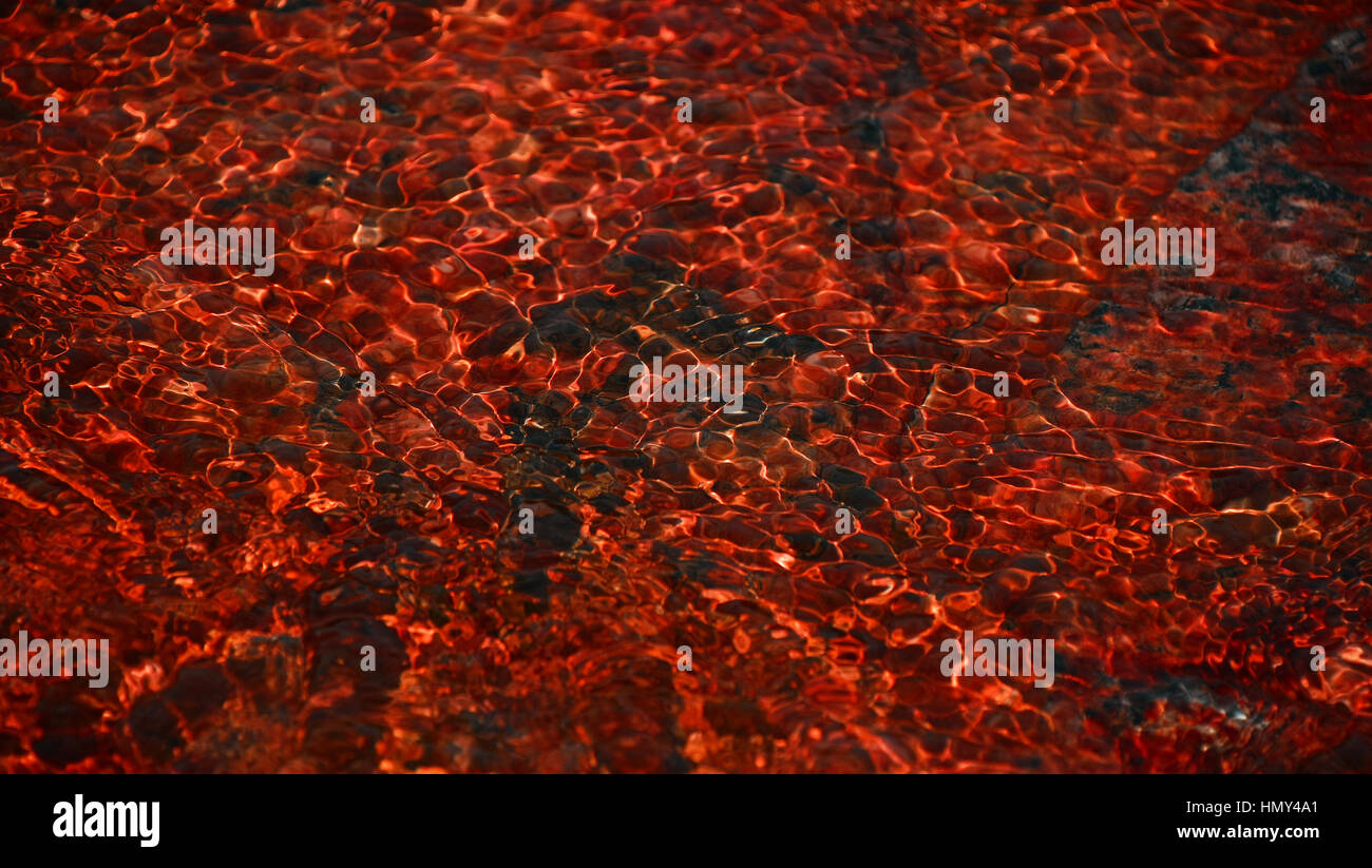Abstract red color running water stream deflection flowing over stones ...