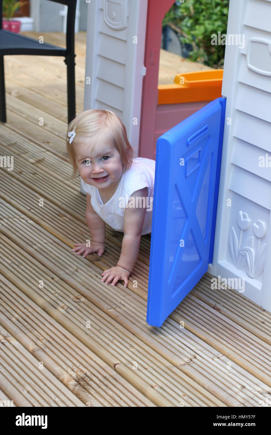 Toddler crawling out of her playhouse, playing in the garden learning ...