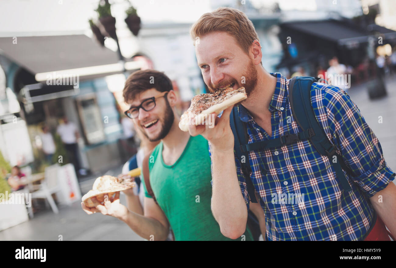 Happy people eating fast food in city while travelling with backpacks ...