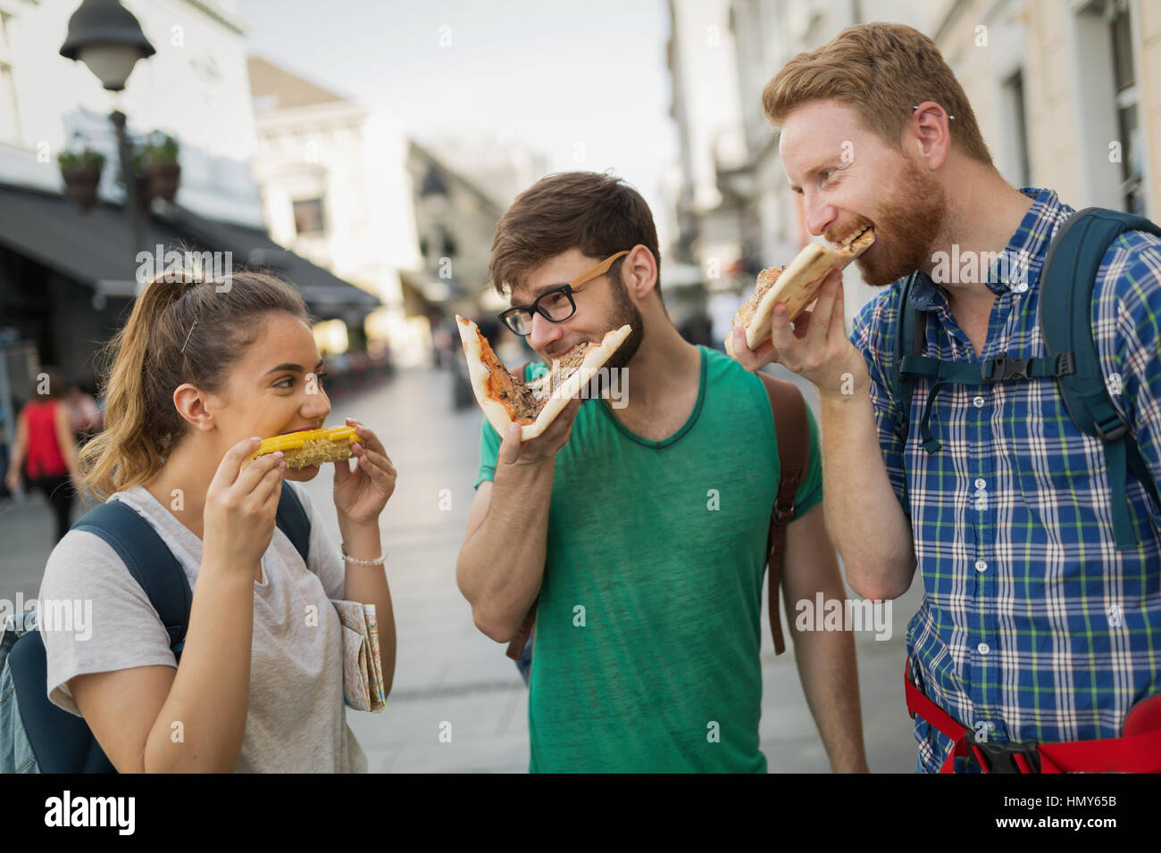 Happy people eating fast food in city while travelling with backpacks ...