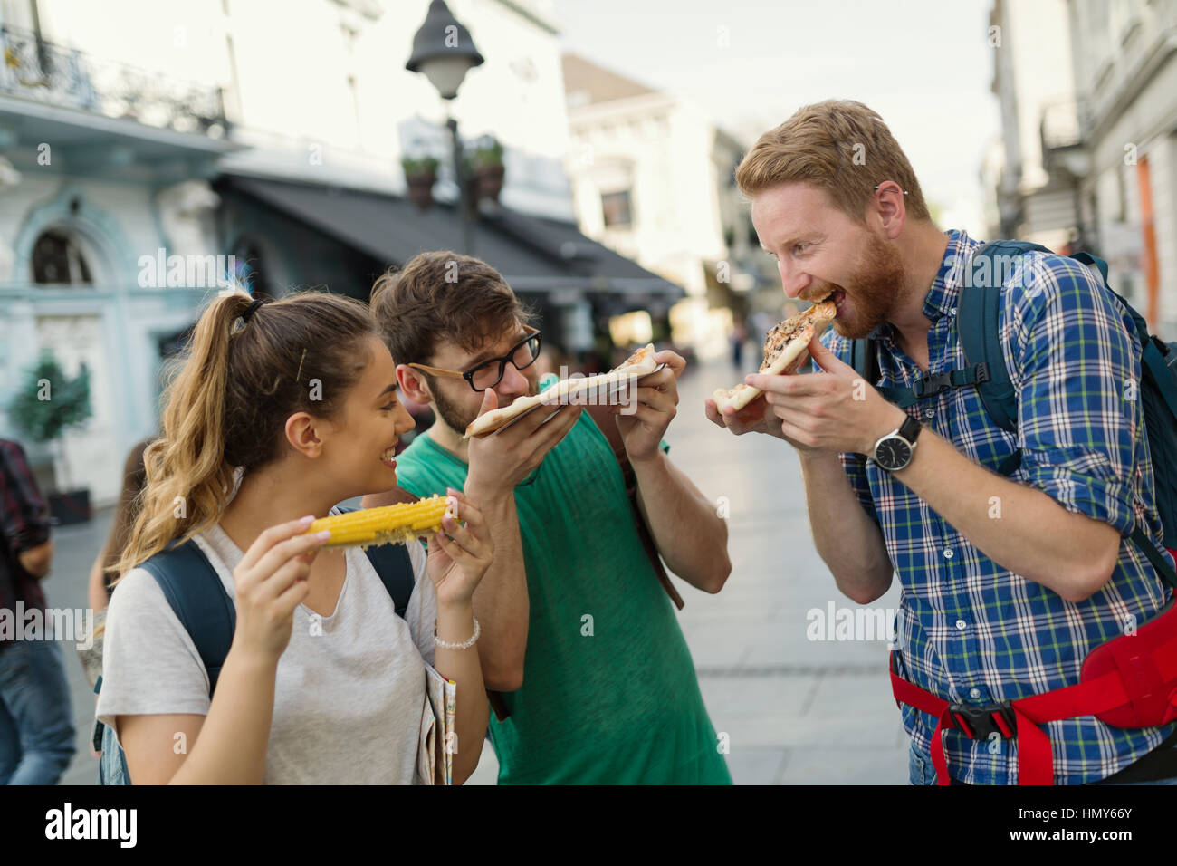Happy people eating fast food in city while travelling with backpacks ...