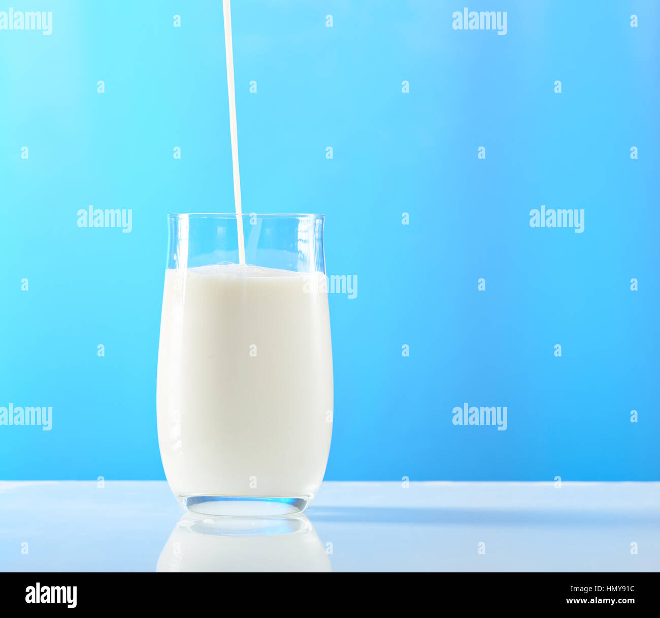 filling up glass with milk isolated on blue background Stock Photo - Alamy