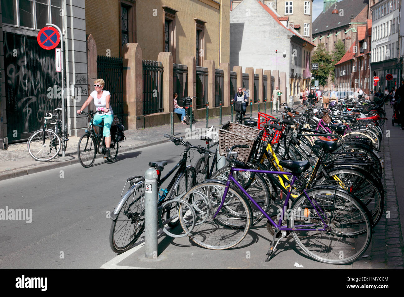 Cyclists and parked bikes in a narrow street in Copenhagen, Denmark ...