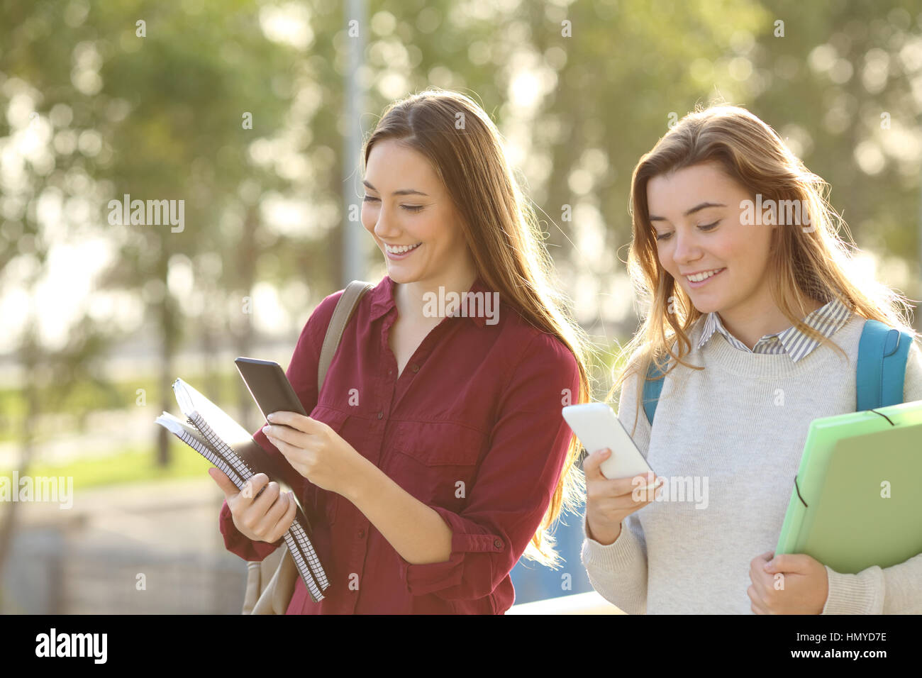 Two happy students walking together and using everyone her smart phone ...