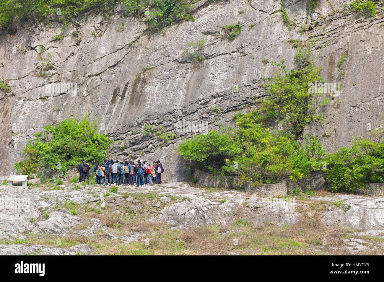 Visitors to former limestone quarry in front of fault in rock face ...