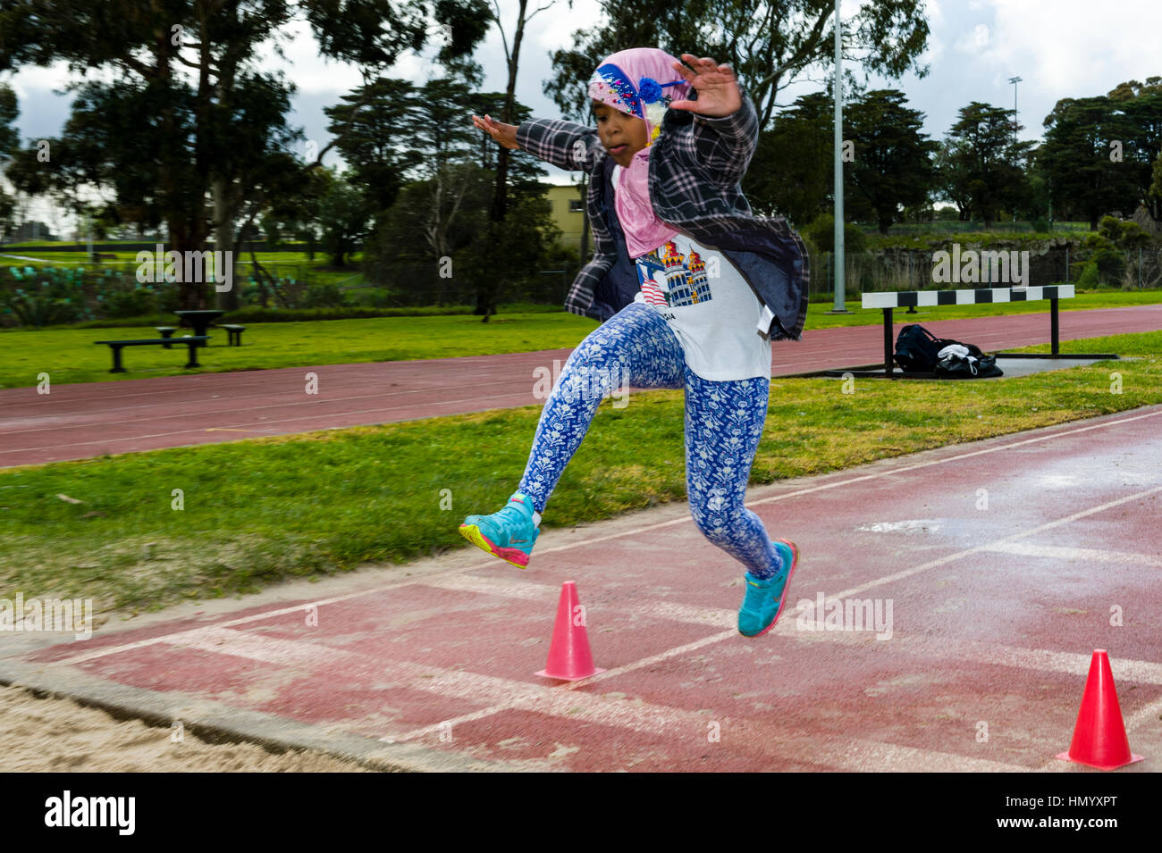 A girl wearing a hijab leaps through the air doing a long jump at an ...