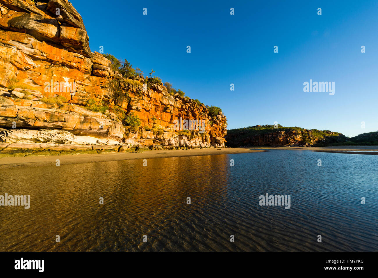 The reflection of orange ochre cliffs in a tidal pool on a beach at ...