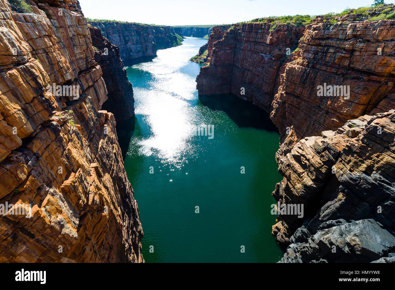 A river flowing beneath sheer ochre sandstone canyon walls on a desert ...