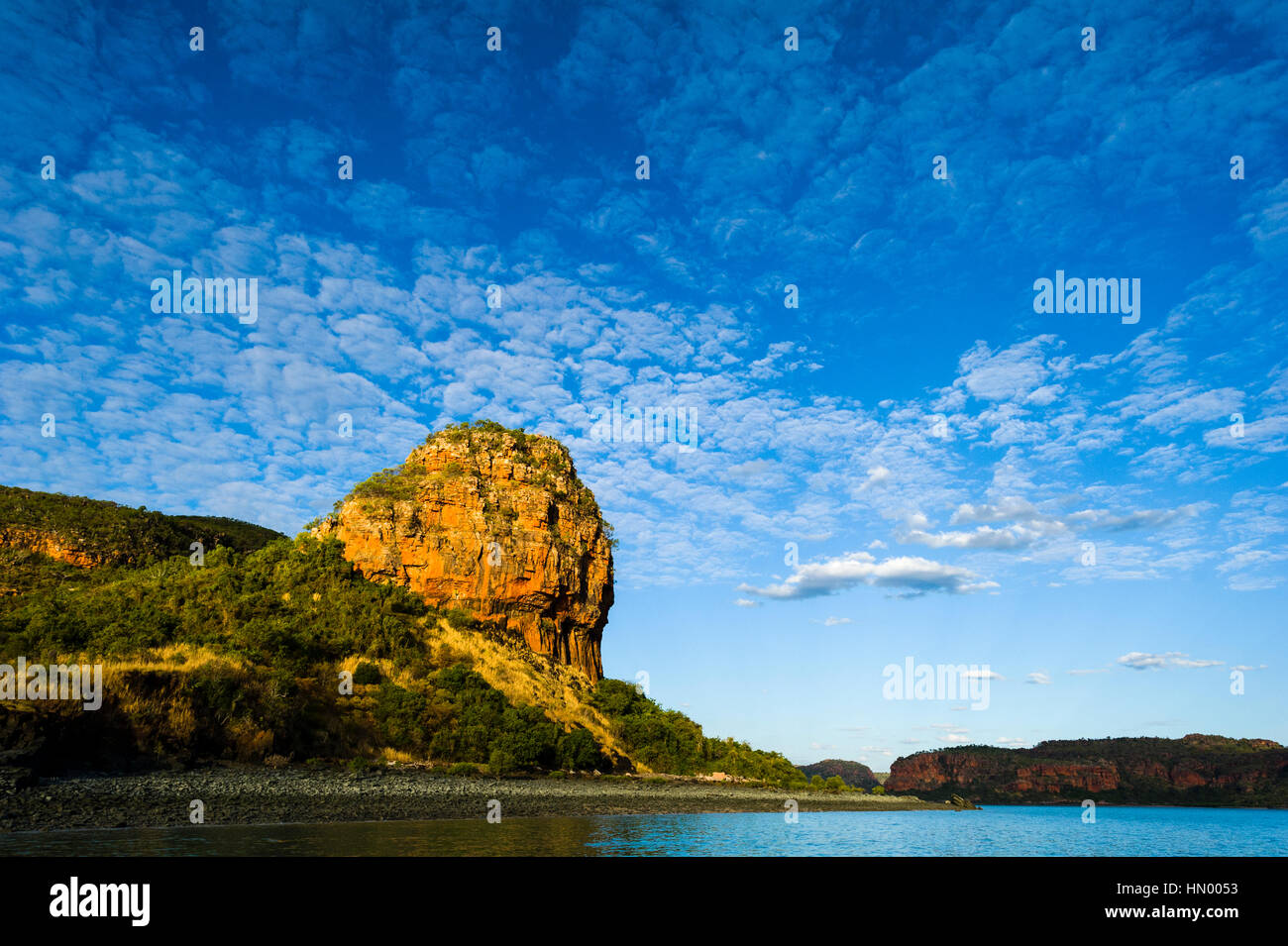 A rugged sandstone headland at the mouth of a river rises into a blue ...