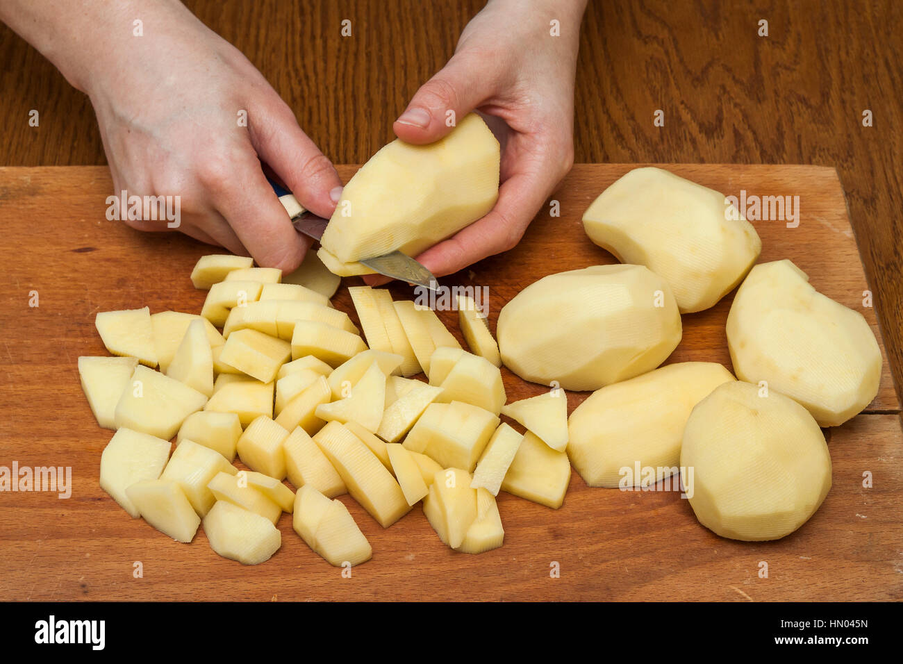 Woman's hand with a knife cutting slicing potatoes on wooden board in ...