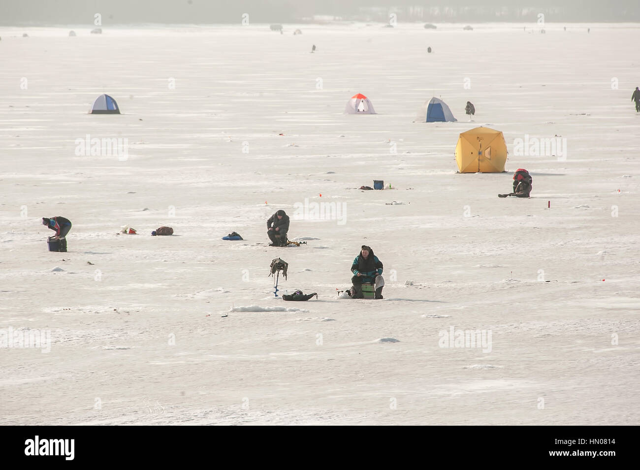 A Russian man on cold winter day as he sits on ice fishing at a river ...