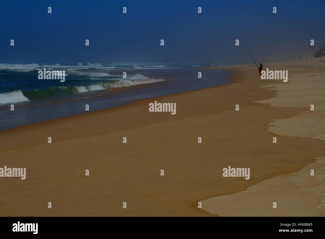 An angler stands fishing with a pole on a deserted beach image in ...