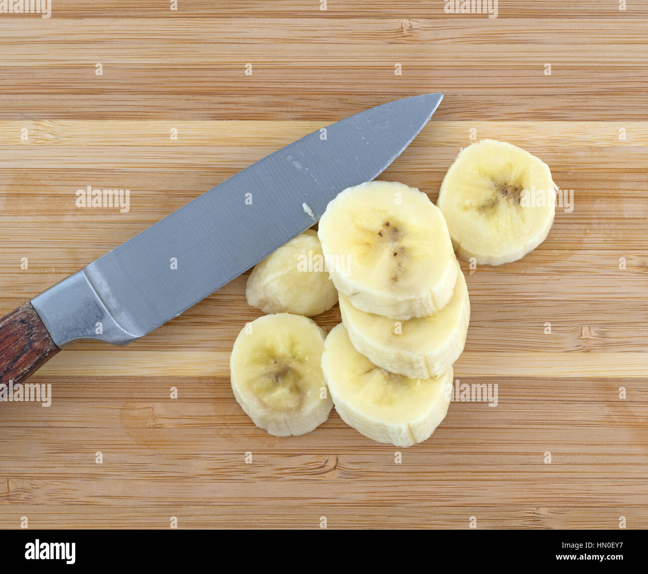 Top close view of sliced bananas on a wood cutting board with a knife ...
