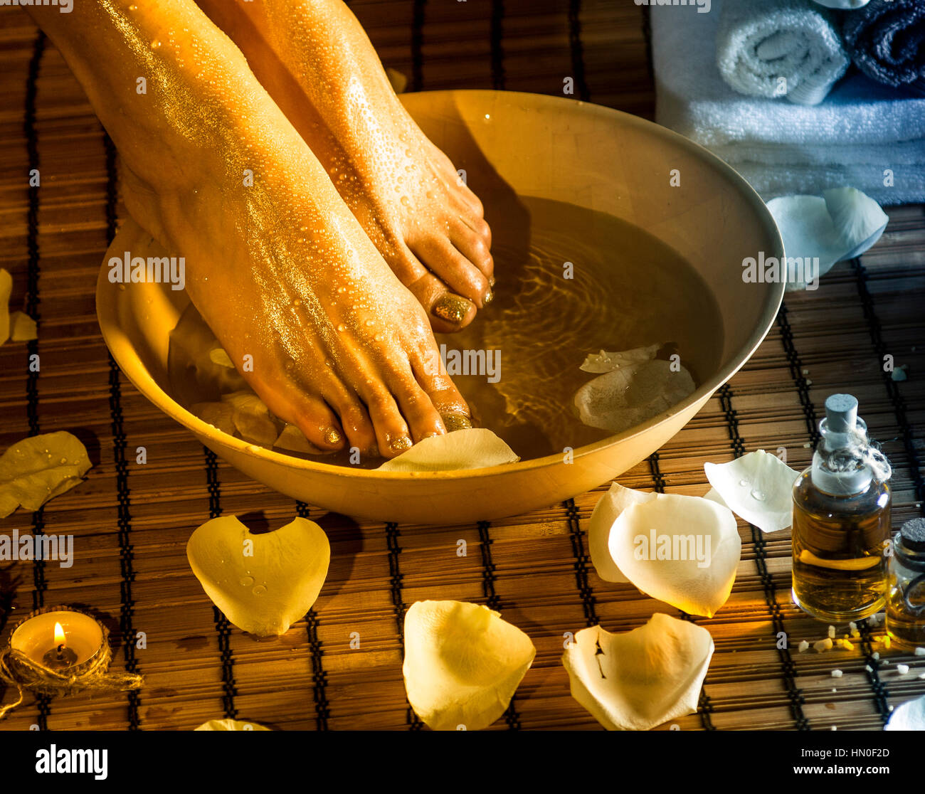 Female feet with drops of water, spa bowl, towels, flowers, candles ...