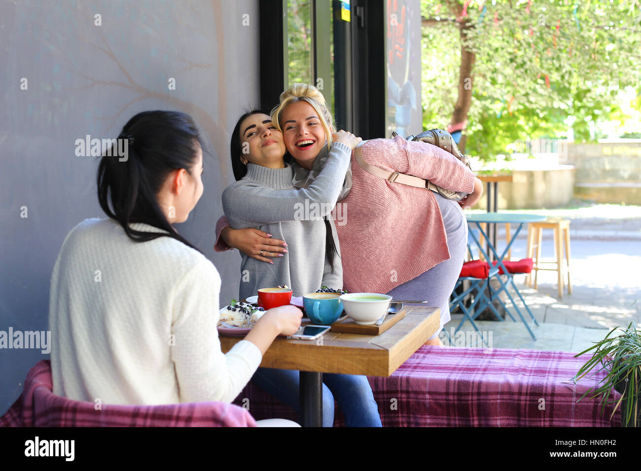 Three young pretty girls girlfriends greet one another, cuddling ...