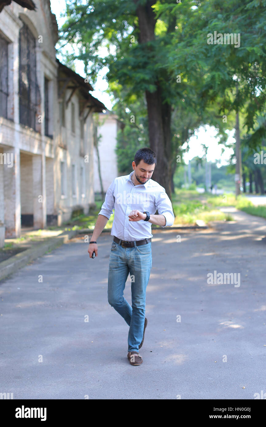 Bearded young men man guy goes, walking along road and looking at watch ...