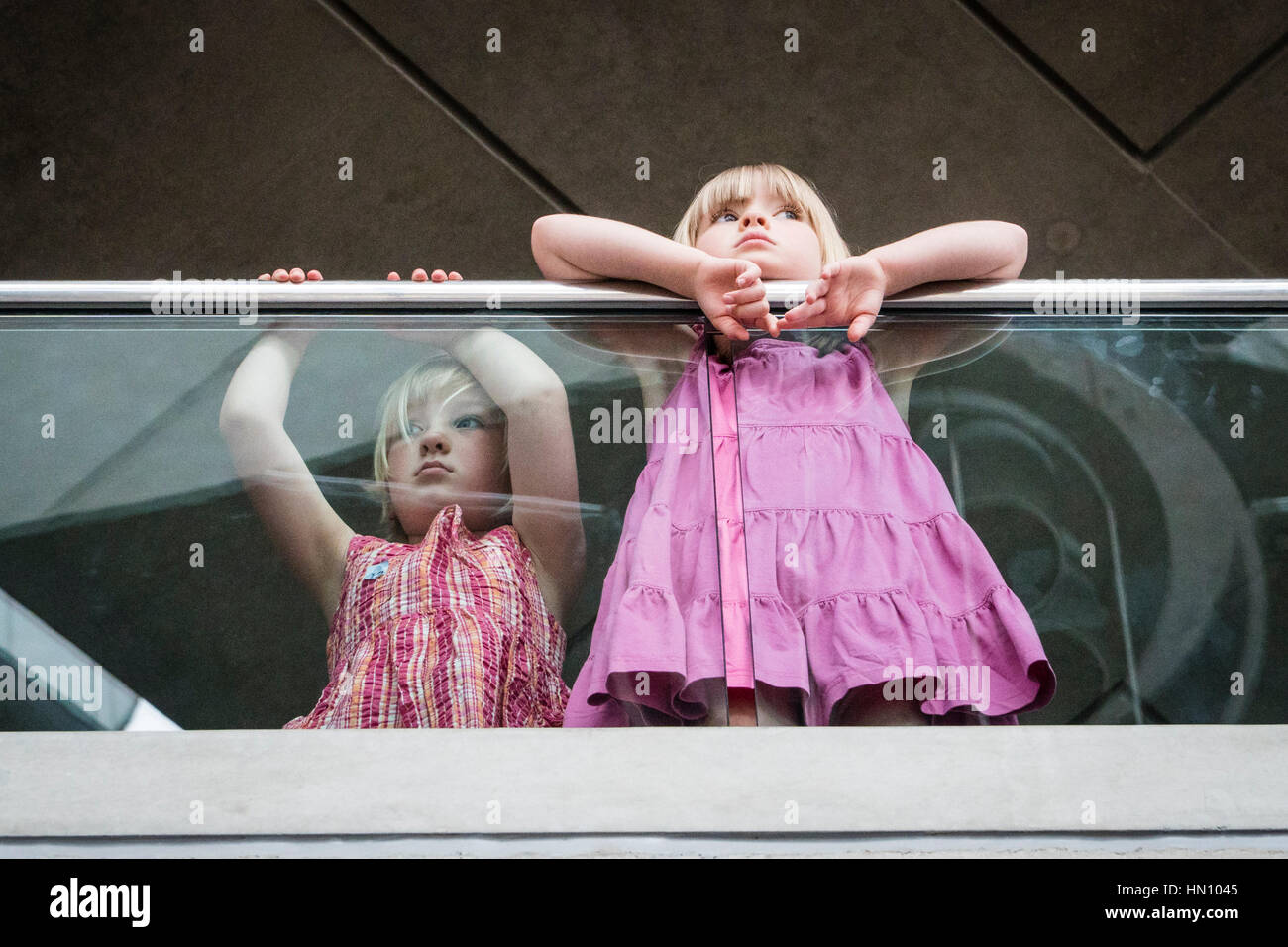 Two young girls peer over and under a glass railing in a museum Stock ...