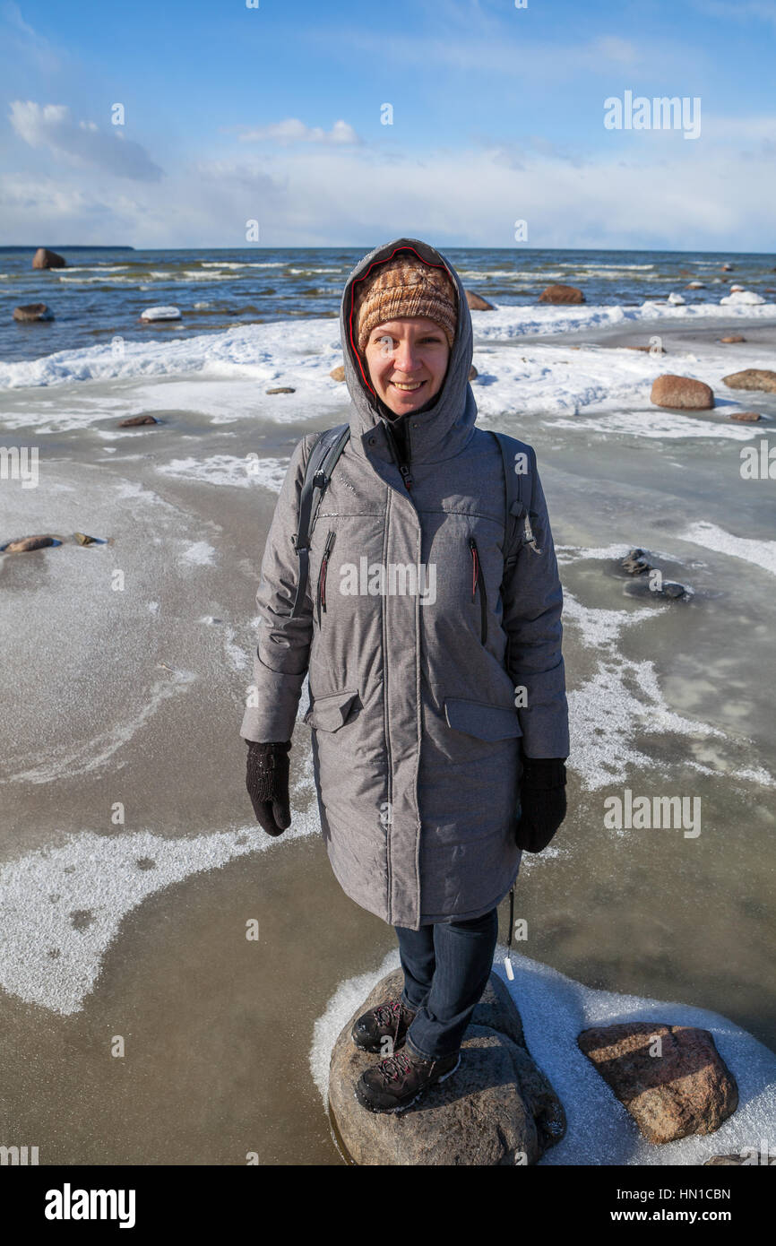 Young smiling woman on the cold and sunny day staying on stone. Coast ...