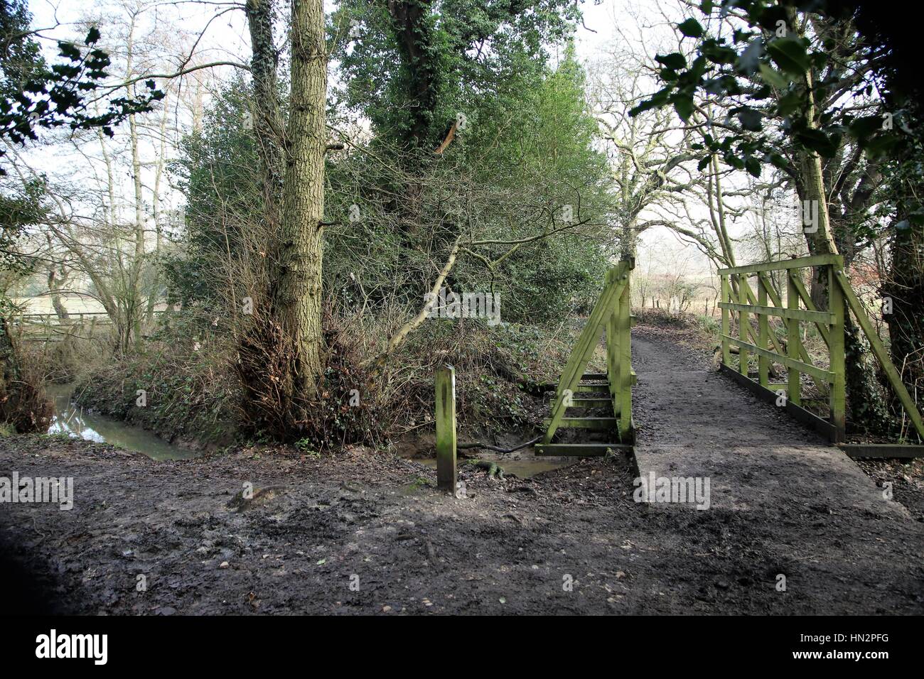 a bridge over a small stream with a muddy footpath in a cold winter ...