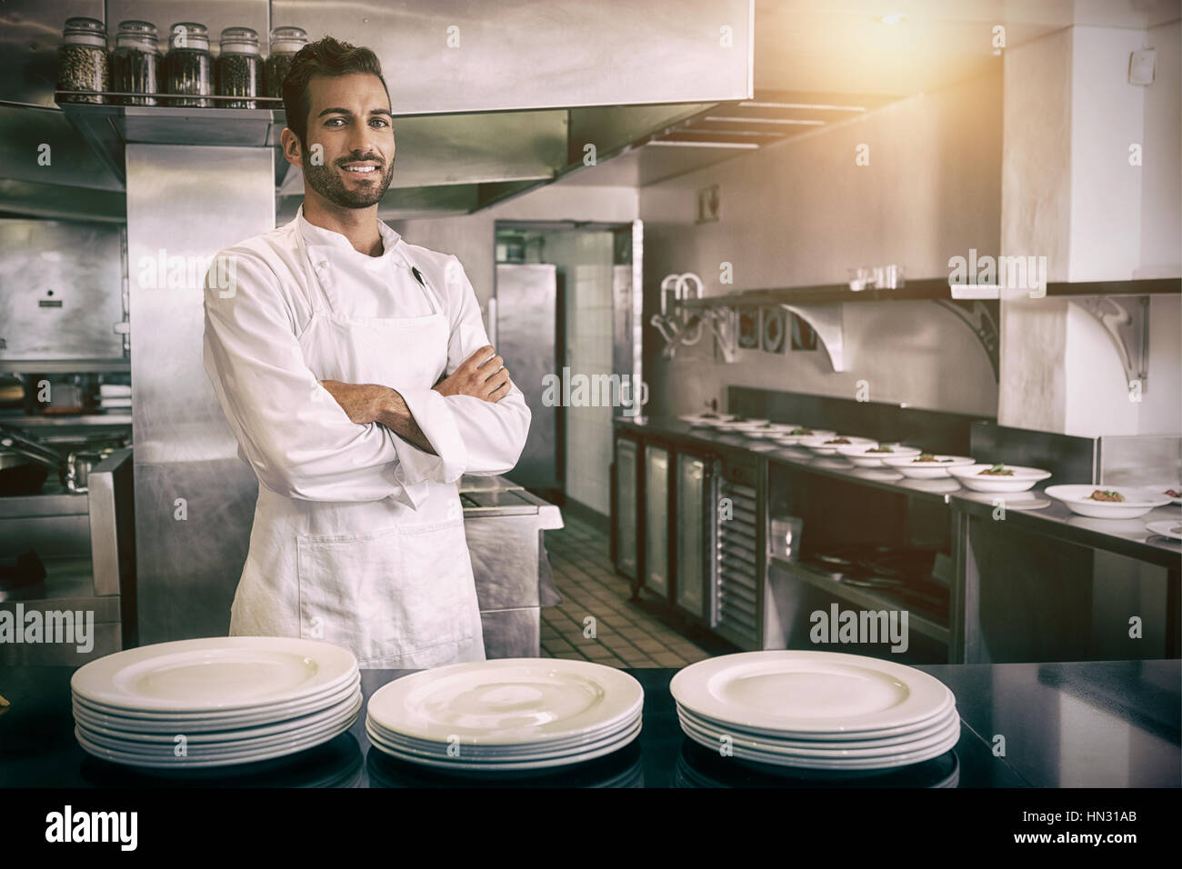 Portrait of smiling young chef standing with arms crossed behind ...