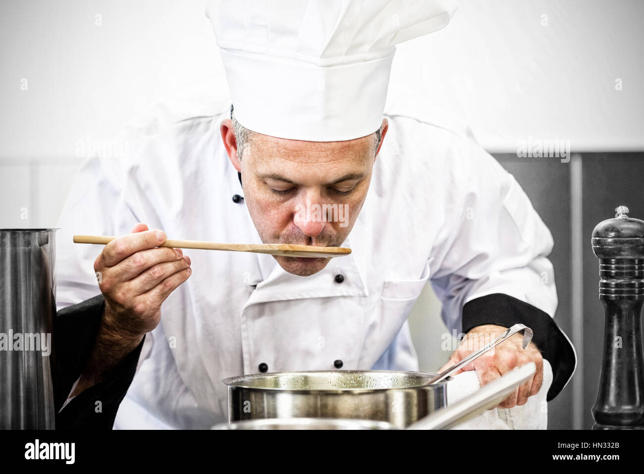 Focused chef tasting sauce with wooden spoon in professional kitchen ...