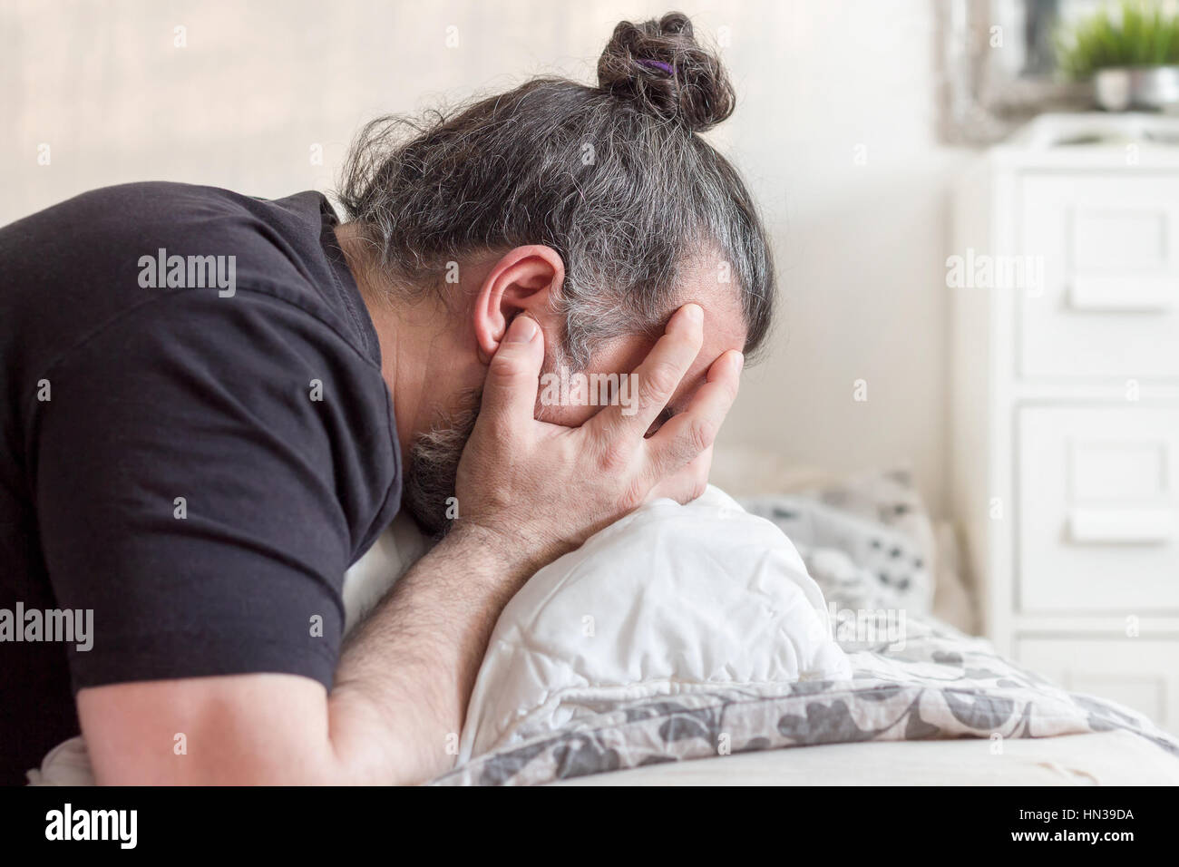 Man covering his face in grief, lying on a bed in bedroom Stock Photo ...