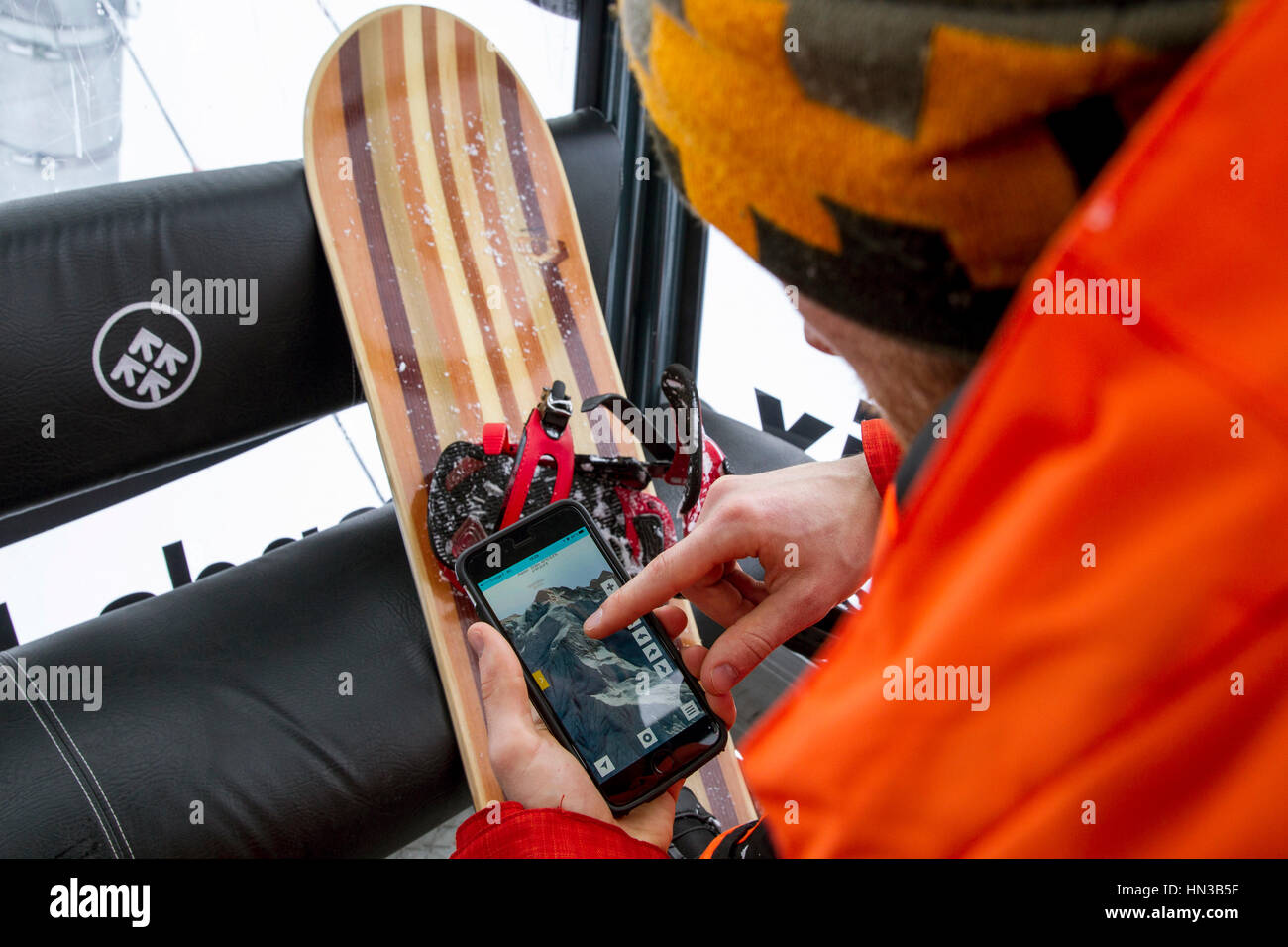 Snowboarder using a phone to check the free ride lines in the lift ...