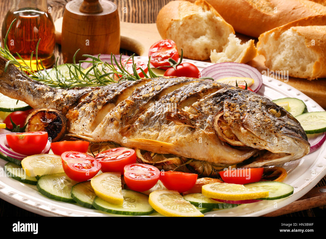 Grilled fish with baguette and vegetables on the plate Stock Photo - Alamy